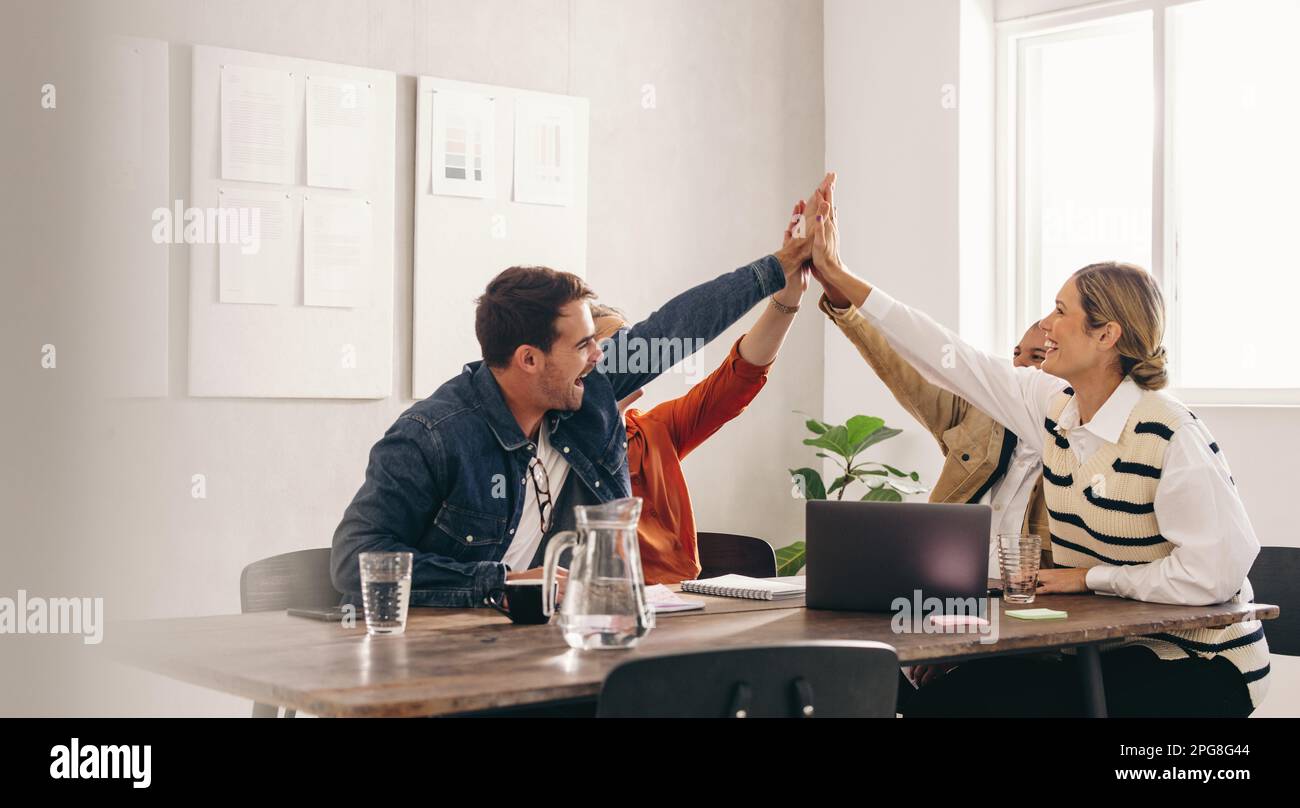 Successful business people smiling and high fiving each other during a meeting in an office ...