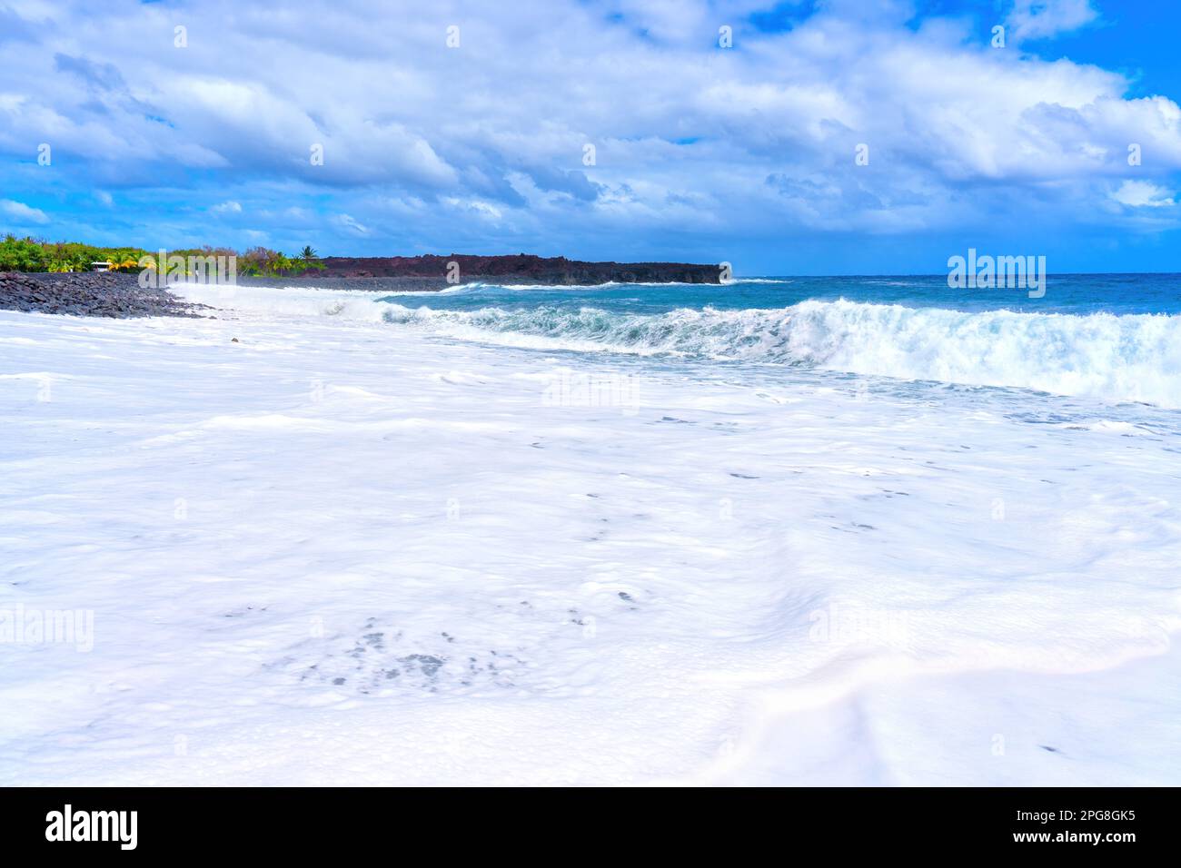 Black sand beach covered in white foam from the ocean waves with thick ...