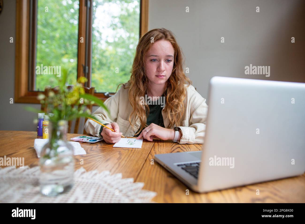 A young woman looking at her laptop and carefully drawing something on ...