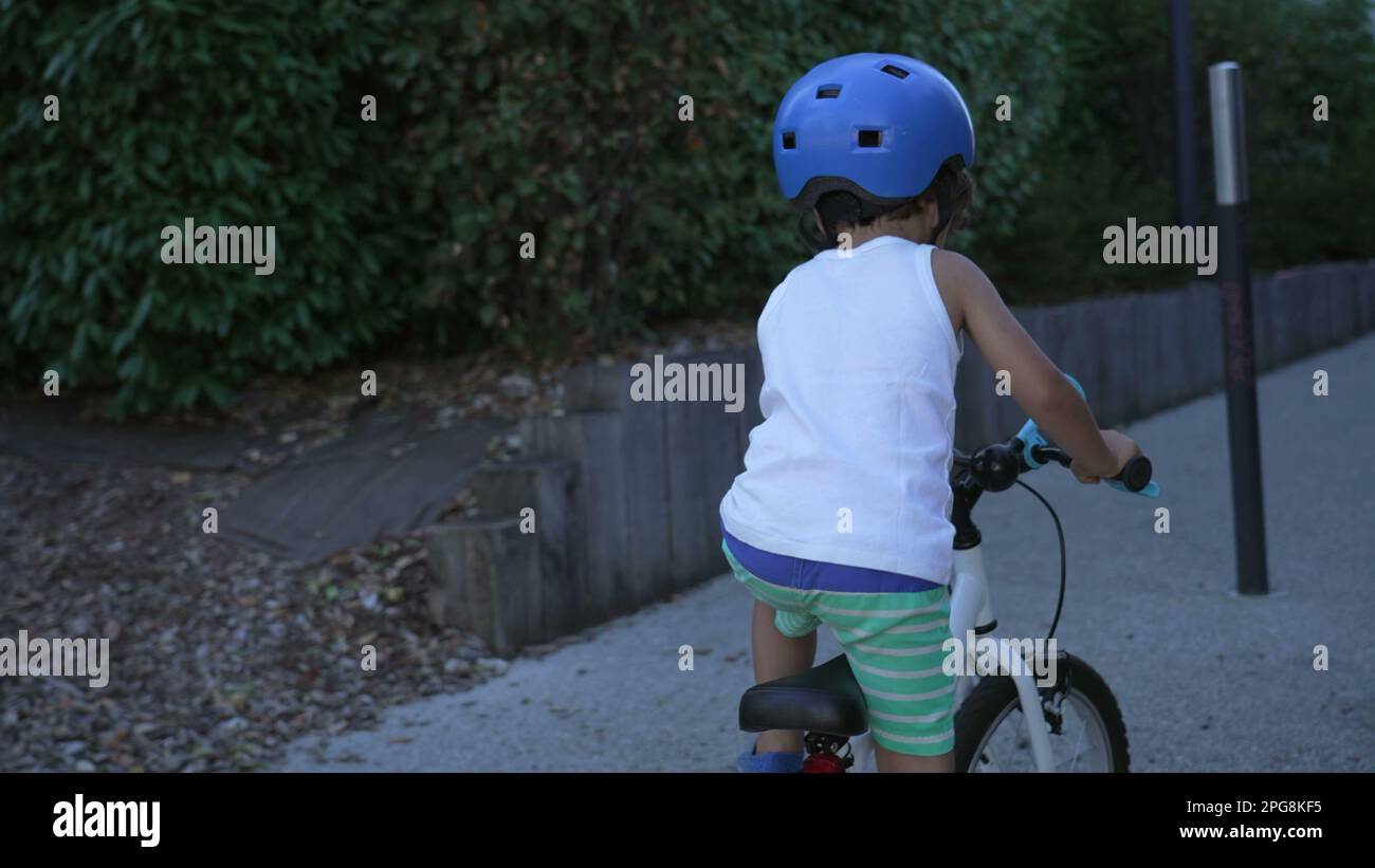 Back of child riding bike and wearing helment outside. Small kid rides ...