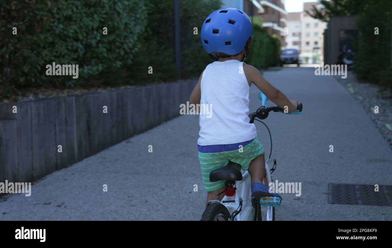 Back of child riding bike and wearing helment outside. Small kid rides ...