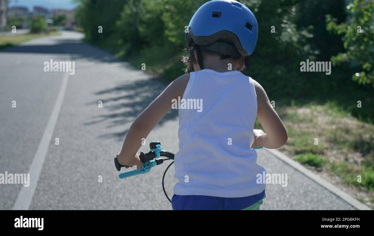 Back of one active child wearing helmet riding bicycle outside in sunny ...