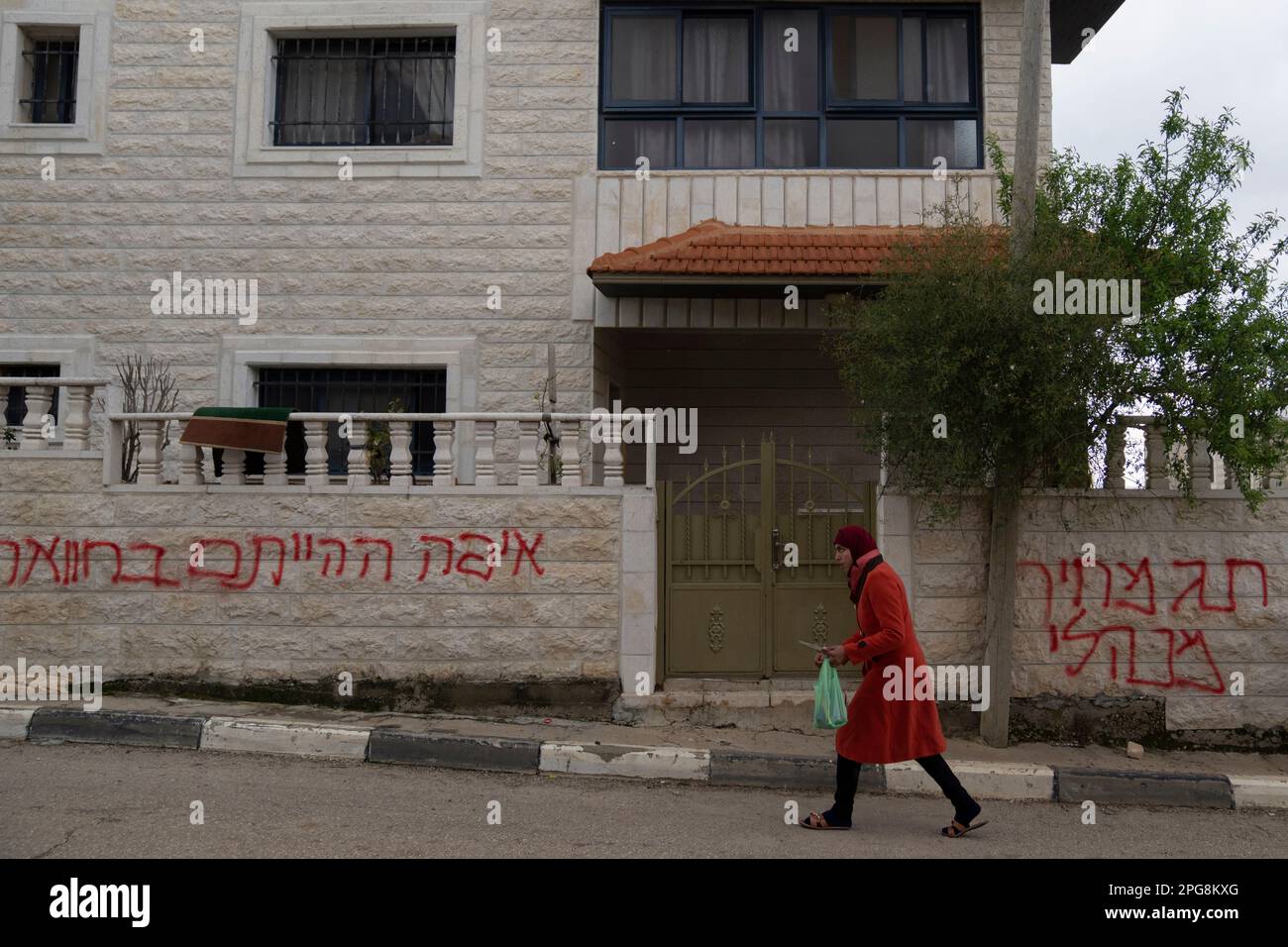 A Palestinian woman walks past a vandalized wall that is sprayed with ...