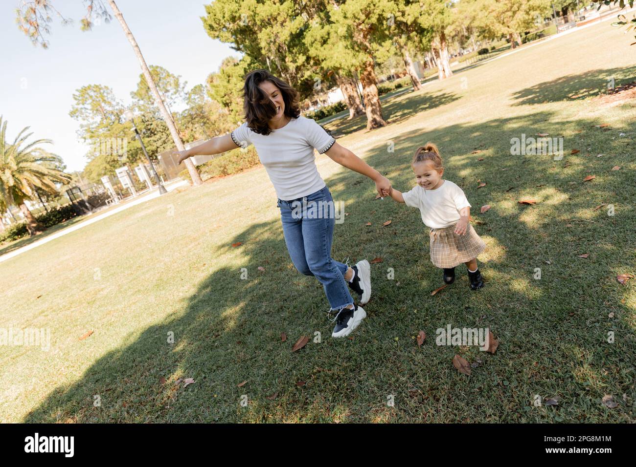 joyful mother and child holding hands while playing together in green ...