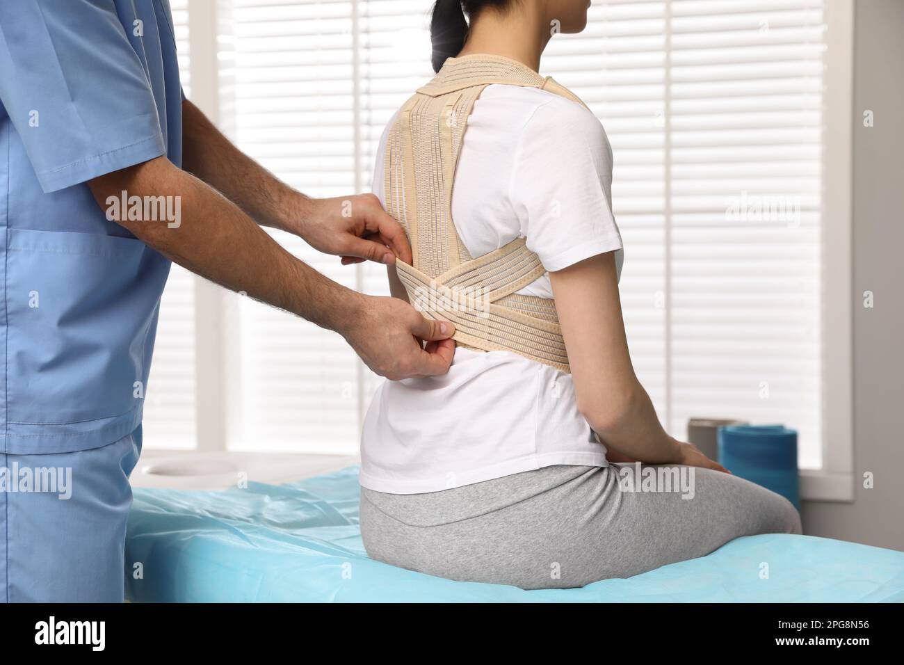 Orthopedist helping patient to put on posture corrector in clinic ...