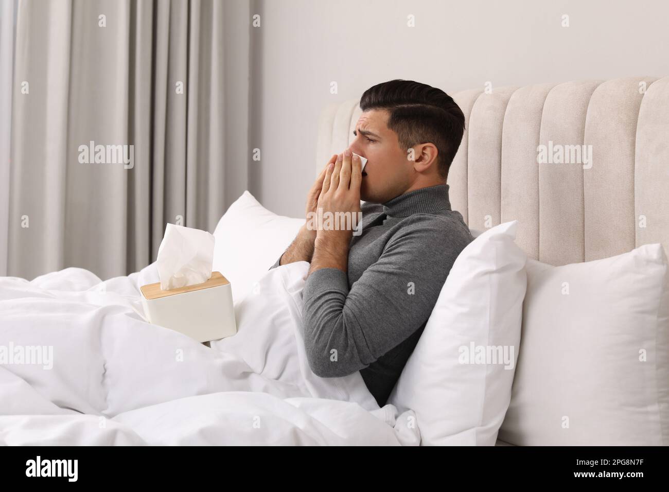 Sick man with box of paper tissues suffering from cold in bed at home ...