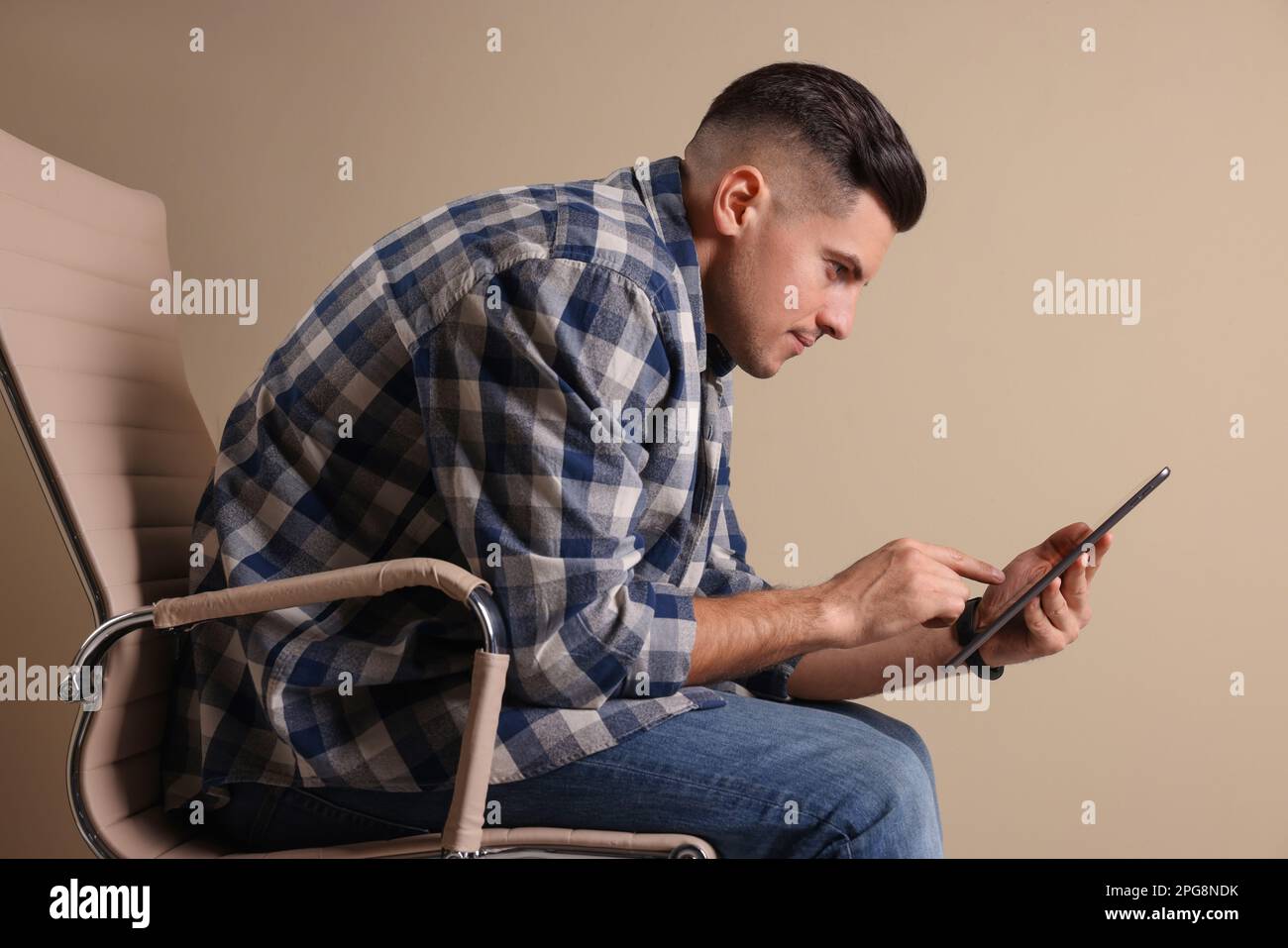 Man with poor posture using tablet while sitting on chair against beige ...