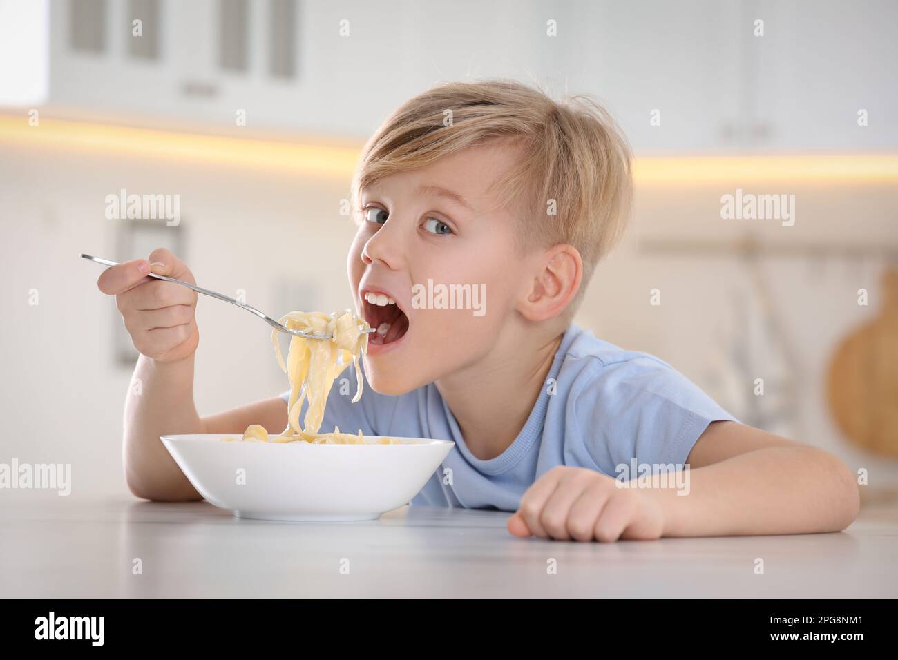 Boy eating tasty pasta at table in kitchen Stock Photo - Alamy