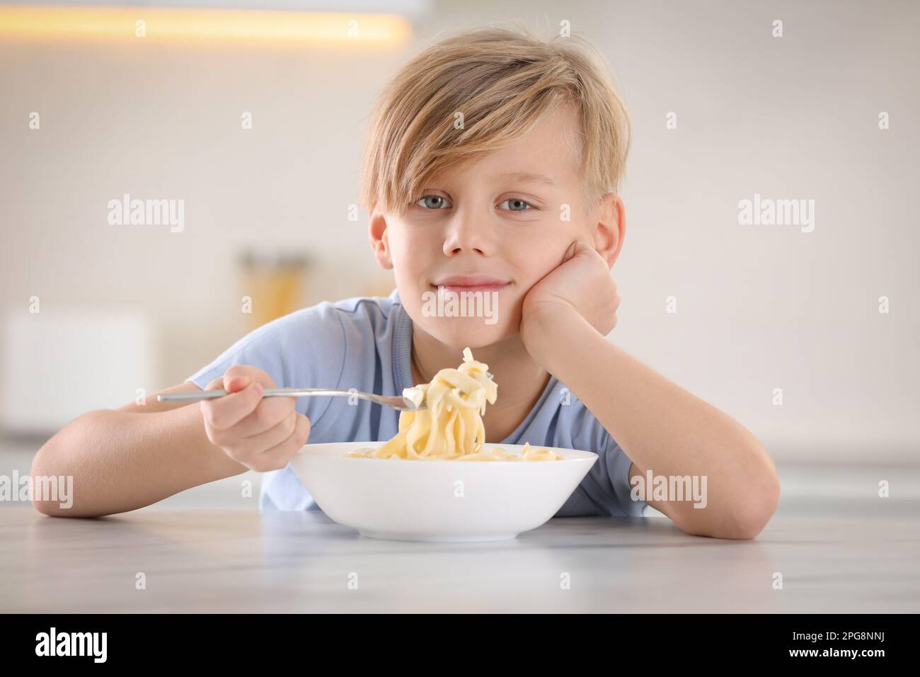 Happy boy eating tasty pasta at table in kitchen Stock Photo - Alamy