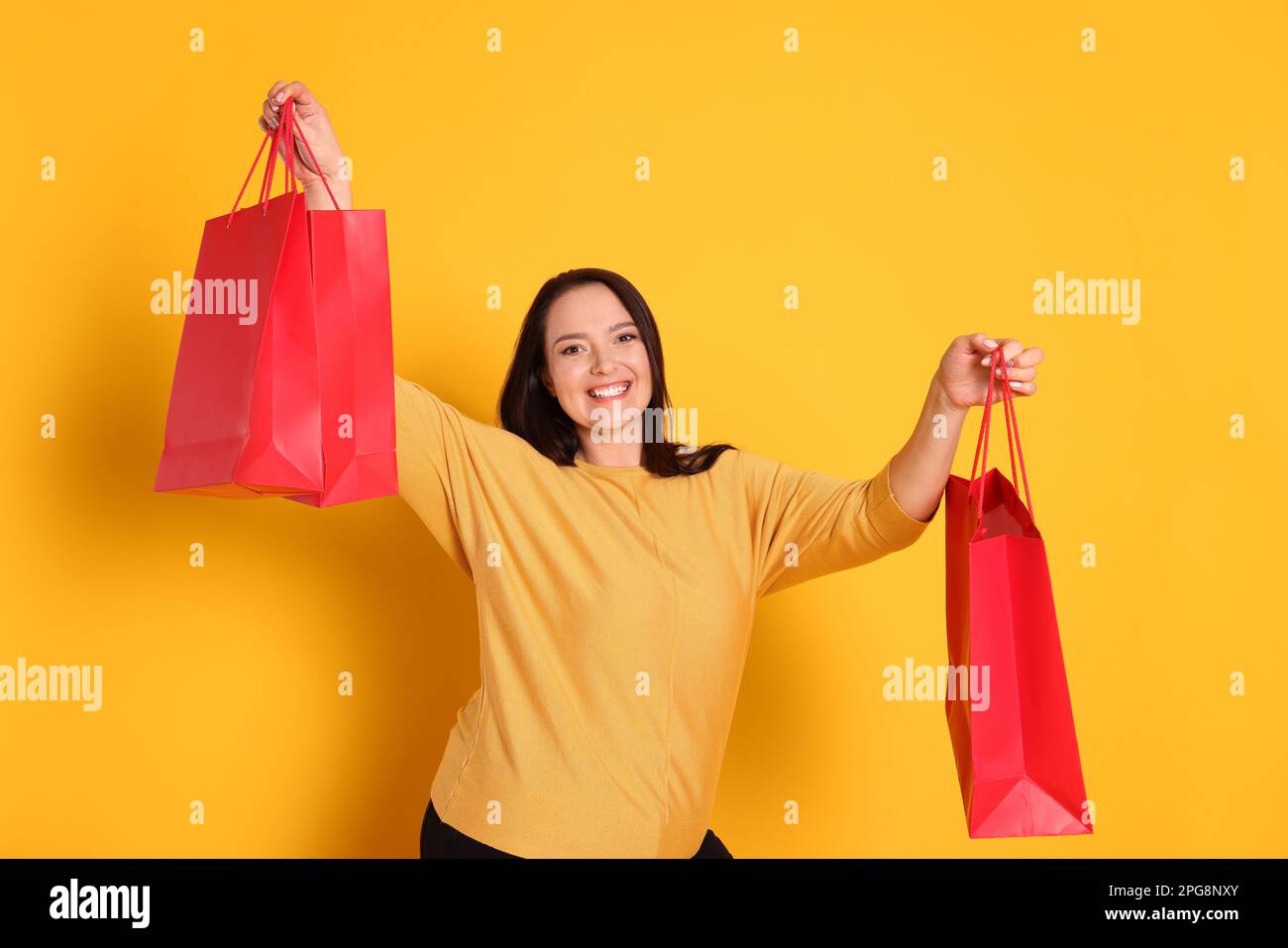 Beautiful overweight woman with shopping bags on yellow background ...