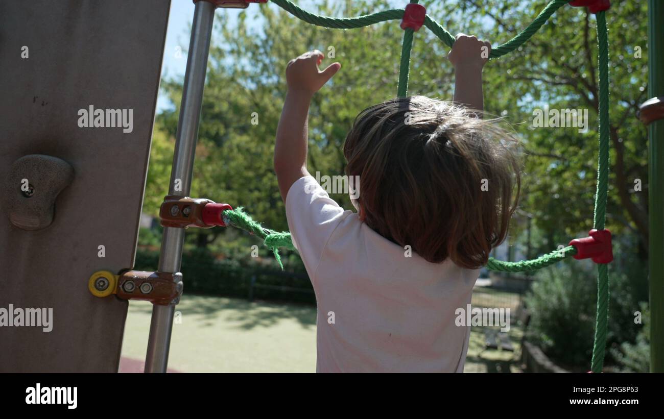 One active child holding into rope ladder at playground outside at city ...