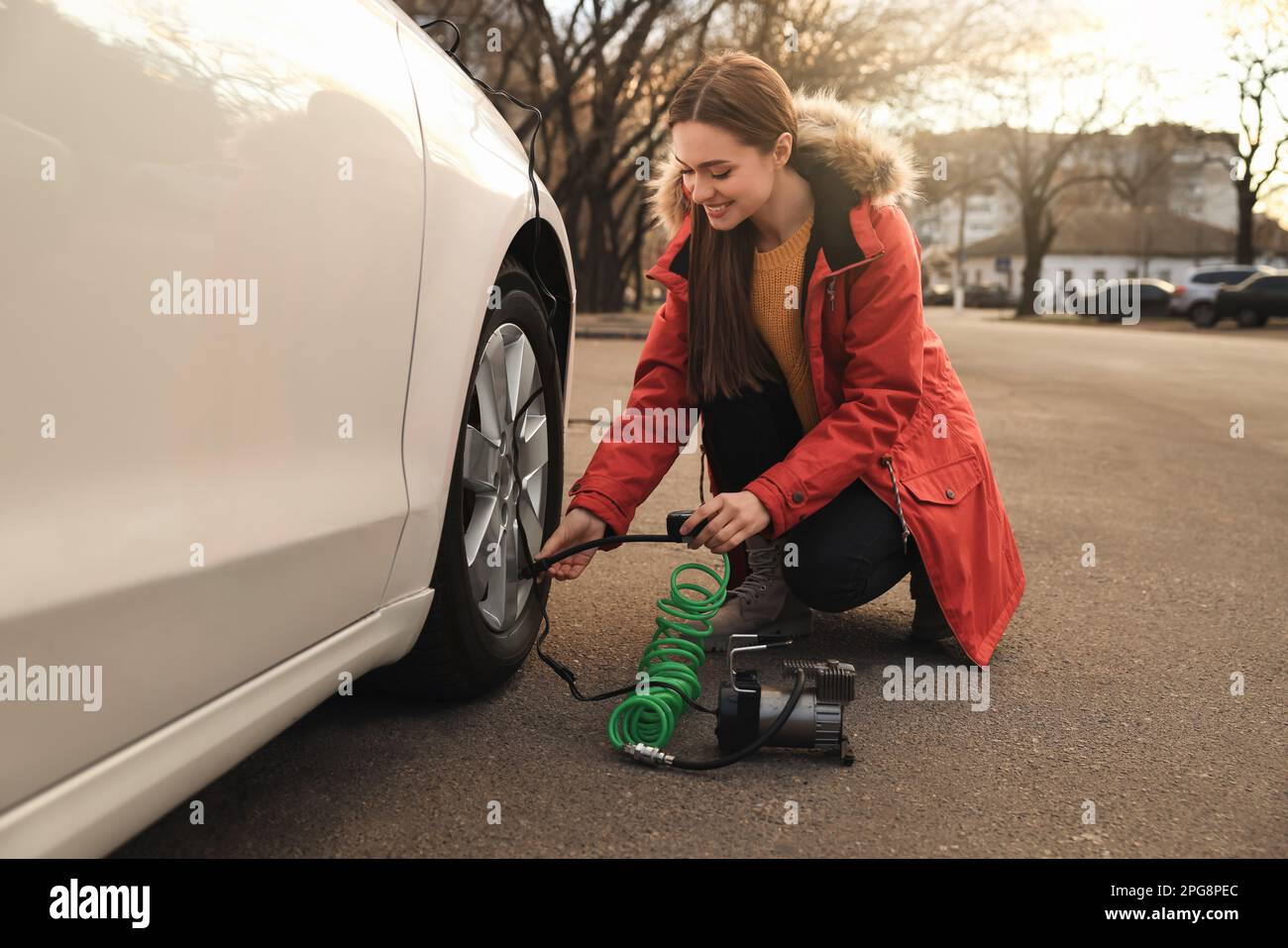Young woman inflating car tire with air compressor on street Stock ...