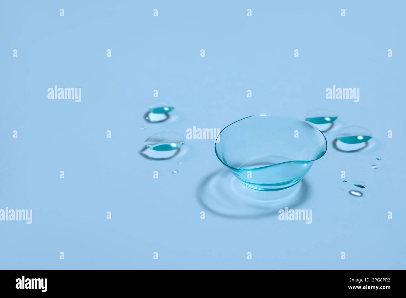 One contact lens and drops of water on light blue background. Space for ...