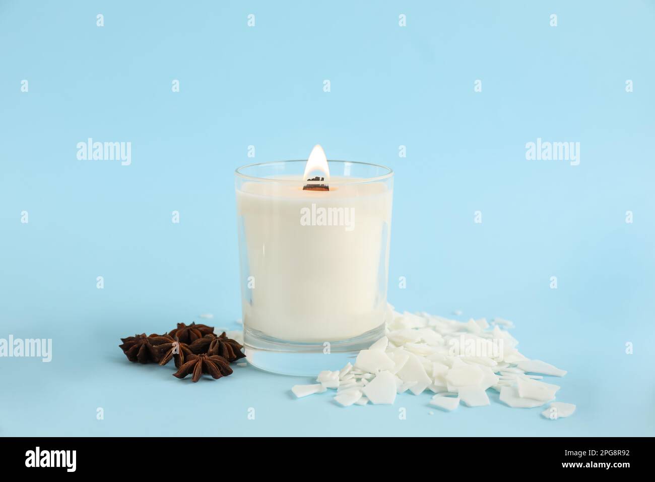 Burning soy candle, wax flakes and anise stars on light blue background ...