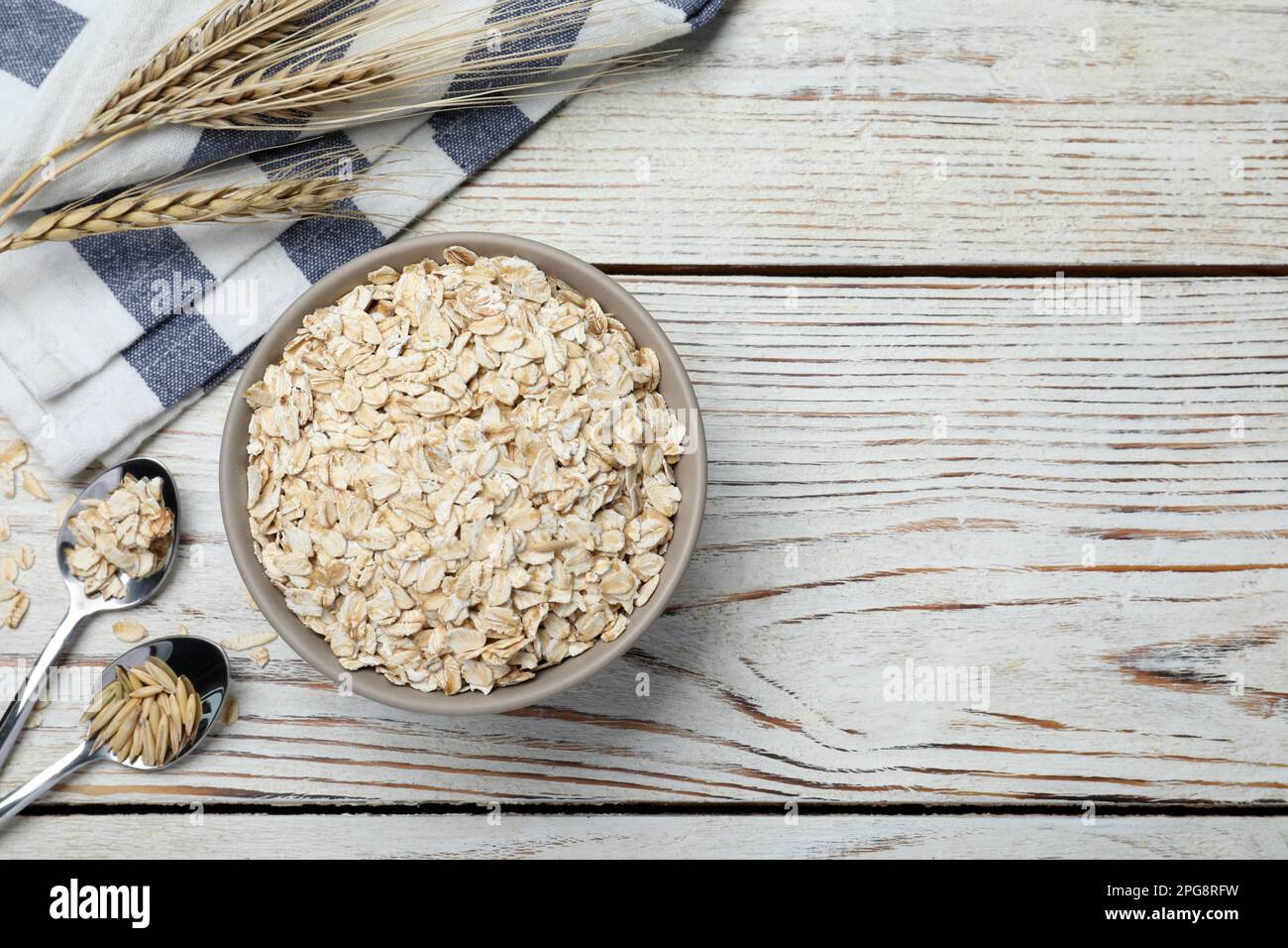Bowl of oatmeal, spoons, napkin and spikelets on white wooden table ...