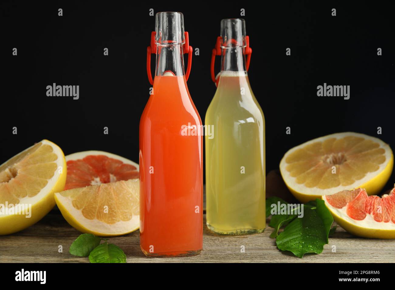 Glass bottles of different pomelo juices and fruits on wooden table ...