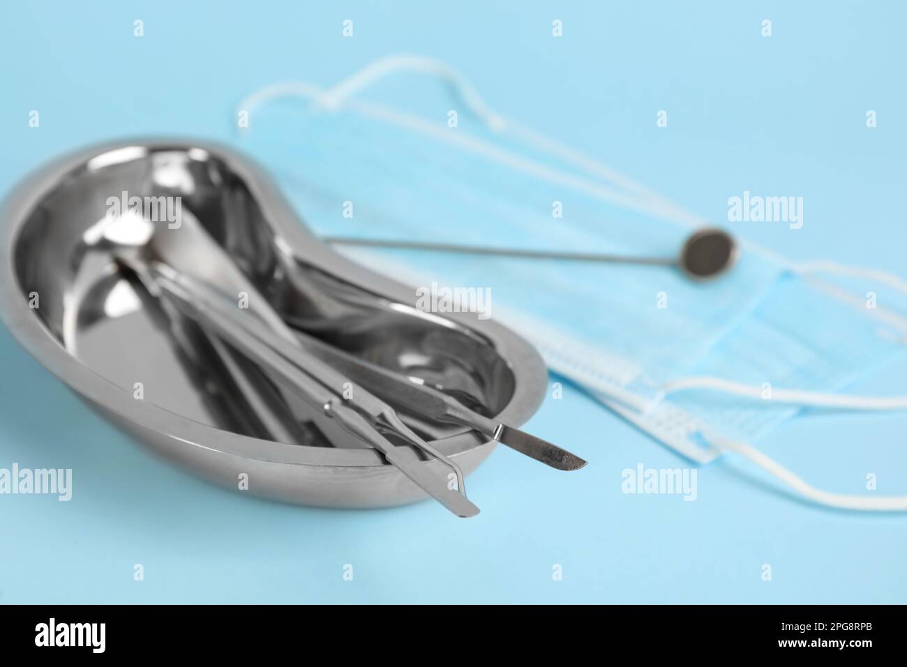 Kidney shaped tray with set of dentist's tools on light blue background ...