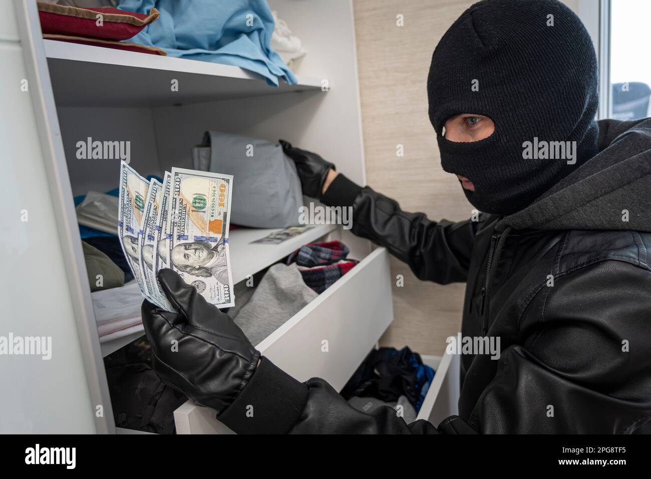 A thief in a black mask searches a closet with clothes in search of ...