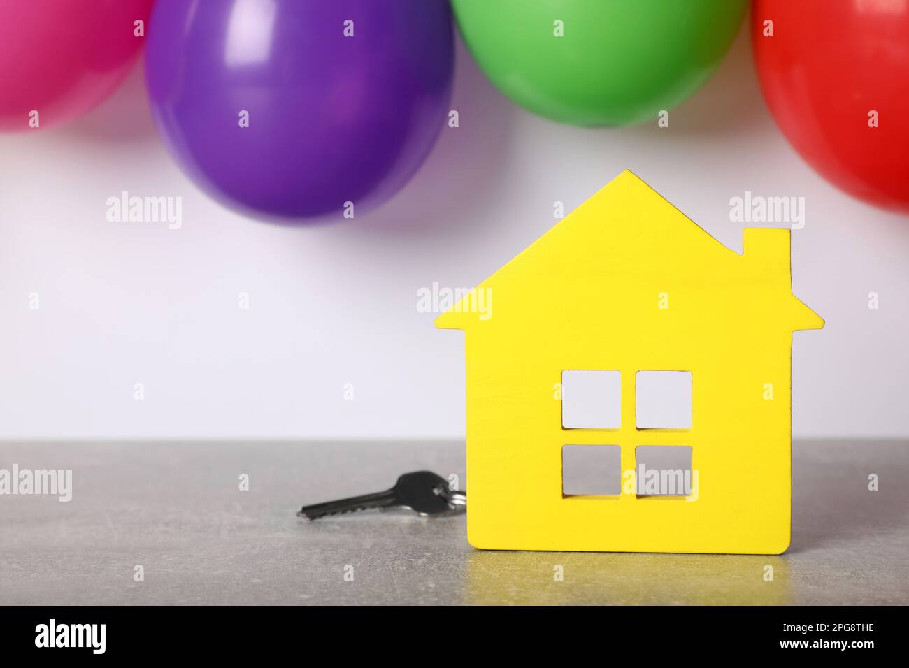 Yellow house model with key and balloons on grey table, space for text ...
