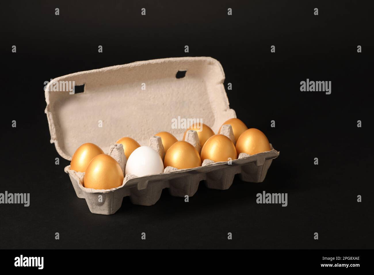 Ordinary chicken egg among golden ones in box on black background Stock ...