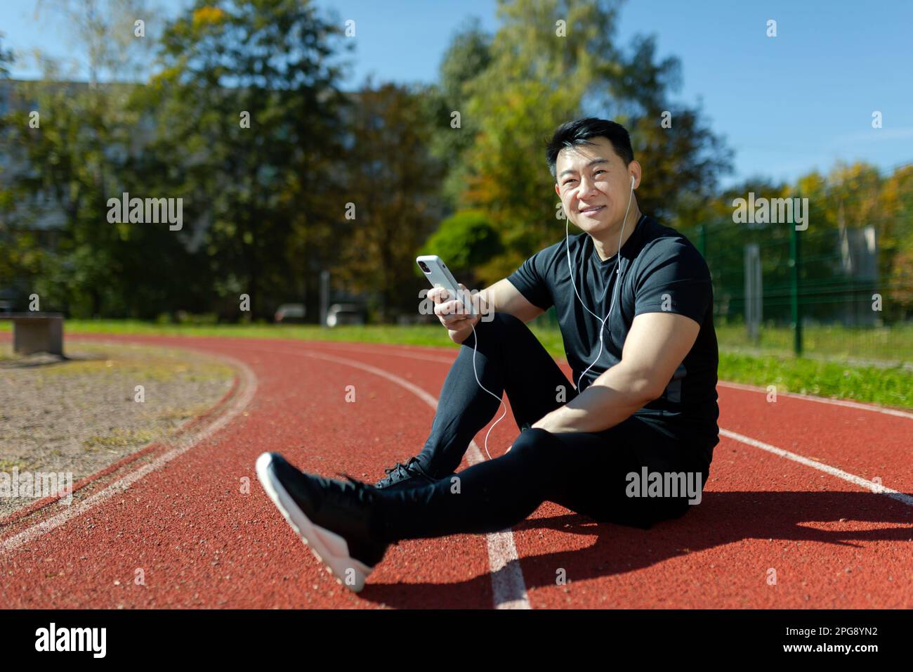 Portrait of a young Asian male athlete sitting in a stadium wearing ...