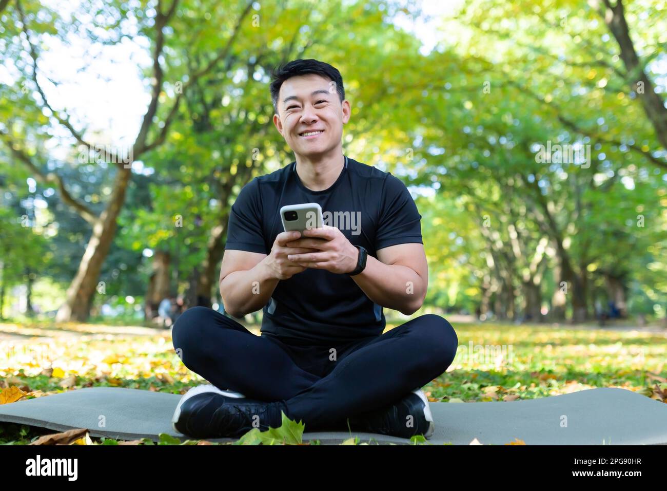 Portrait of a young Asian male athlete, coach sitting in the park on a ...