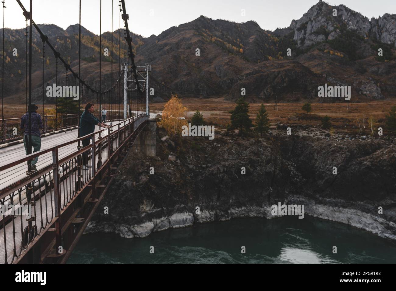 Two women walk on a bridge across the mountain river Katun with rocky ...