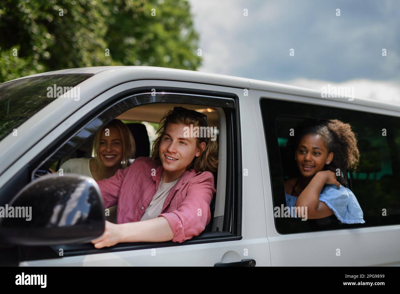 Multiracial young friends travelling together by car, looking through ...
