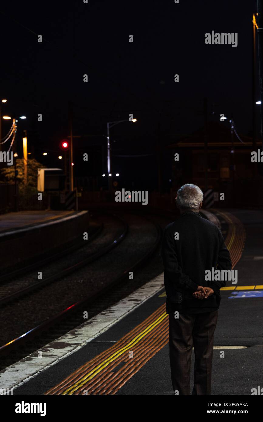 An old man standing alone next to the traintracks waiting for the train ...