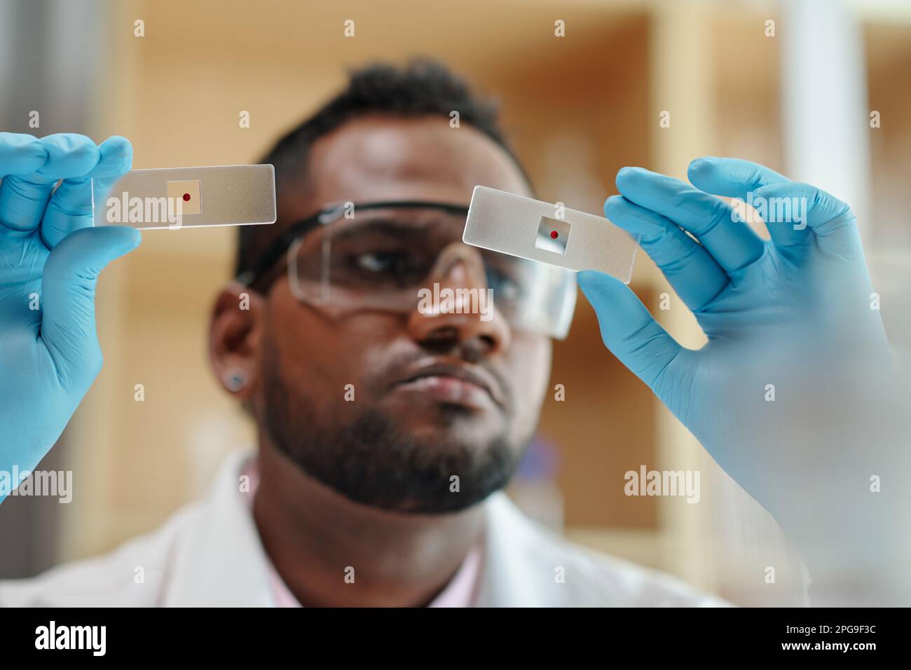 Focus on gloved hands of young male scientist holding slides and ...