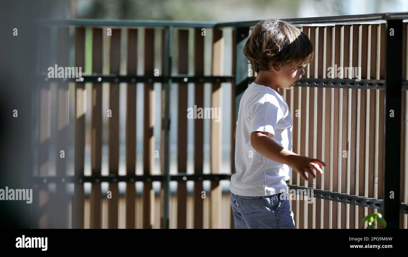 Child standing by balcony fence looking outdoors from second floor ...