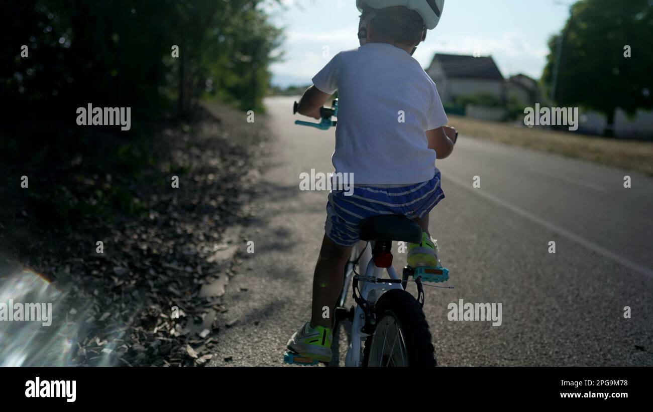Back of child learning to ride bike wearing helmet in bicycle urban ...