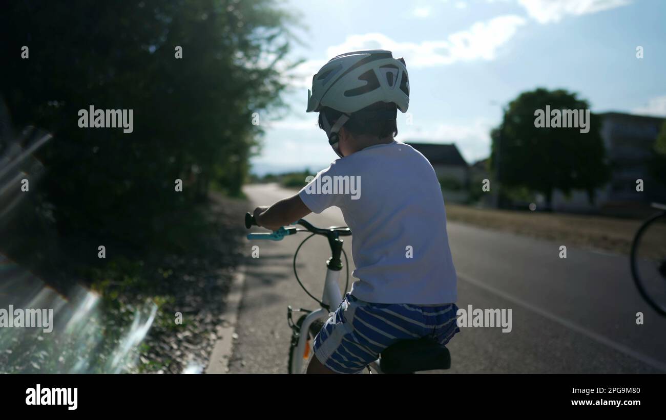 Back of child learning to ride bike wearing helmet in bicycle urban ...
