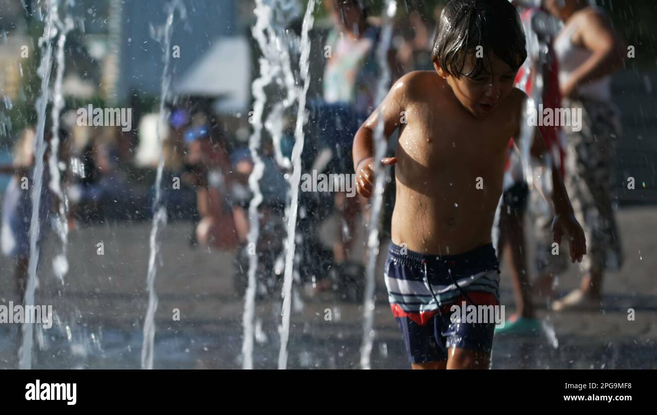 Little boy running toward water jet fountain. Kid having fun at water ...