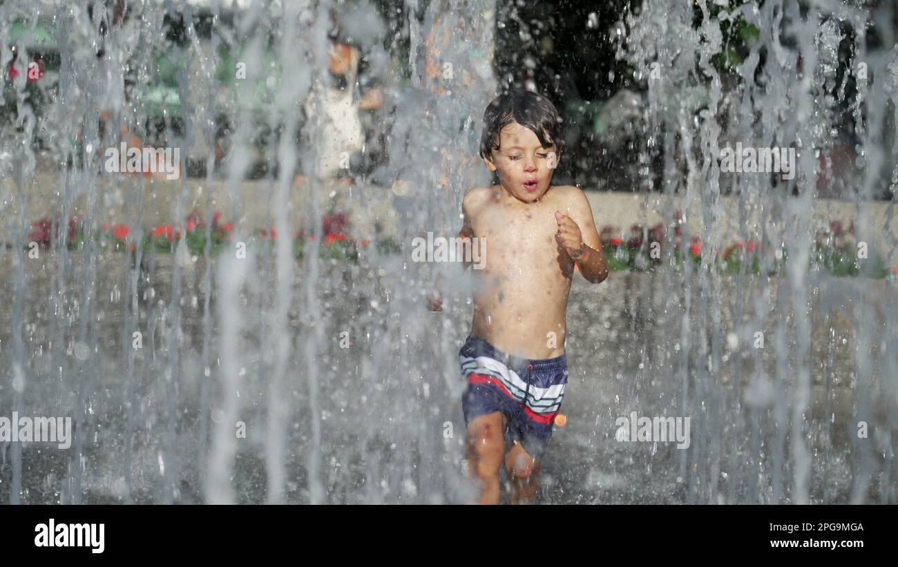 Little boy running at water jets in city park during summer day. Small ...