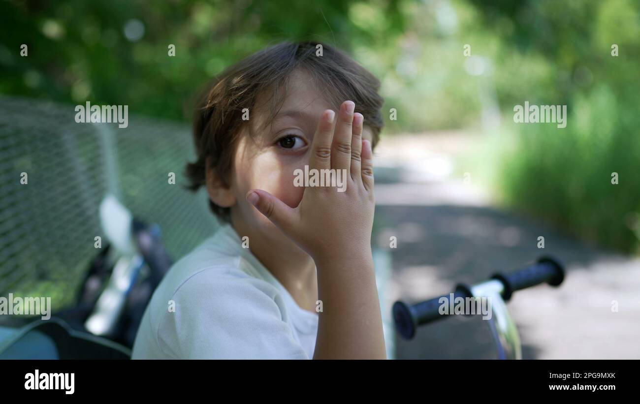 Little boy rubbing nose with hand seated at park bench. Kid touching ...