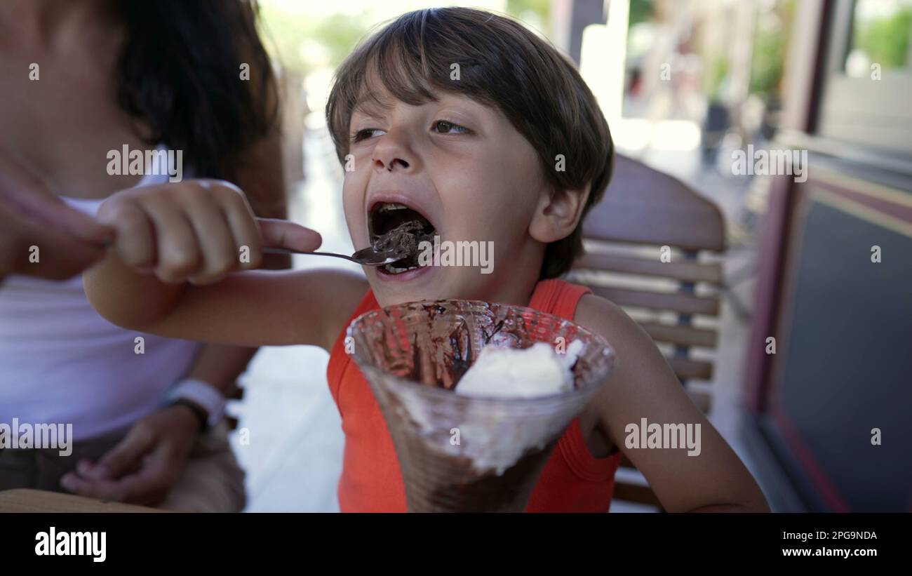 Small child eating chocolate ice cream with whipped cream with spoon at ...