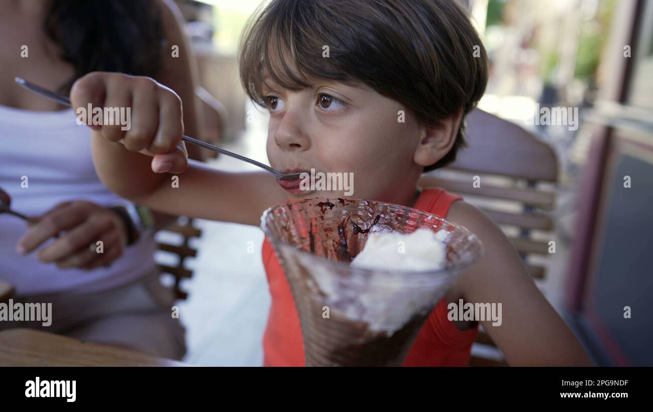 Small child eating chocolate ice cream with whipped cream with spoon at ...