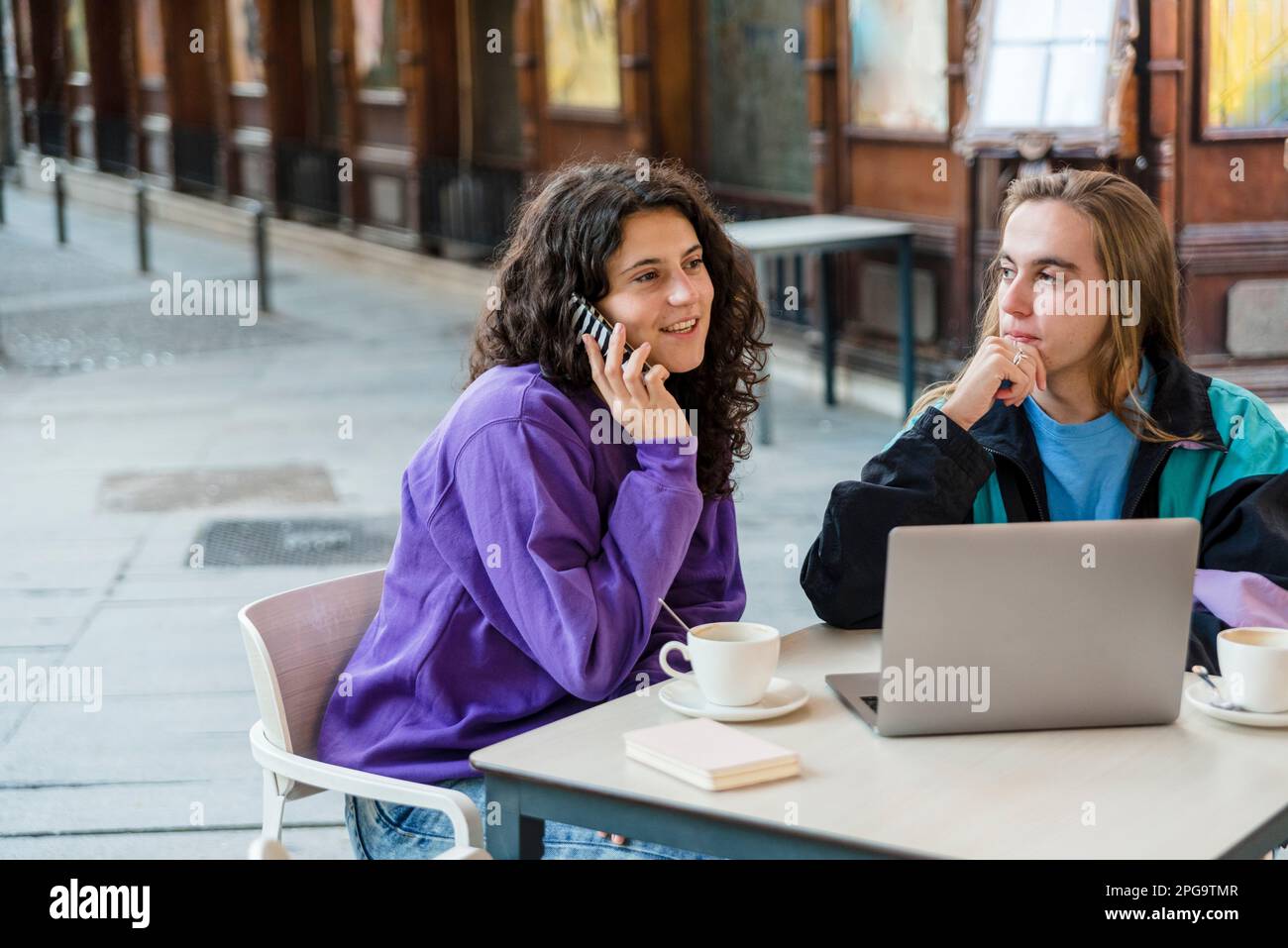 Two people using laptop and mobile phone while sitting outdoors at a ...