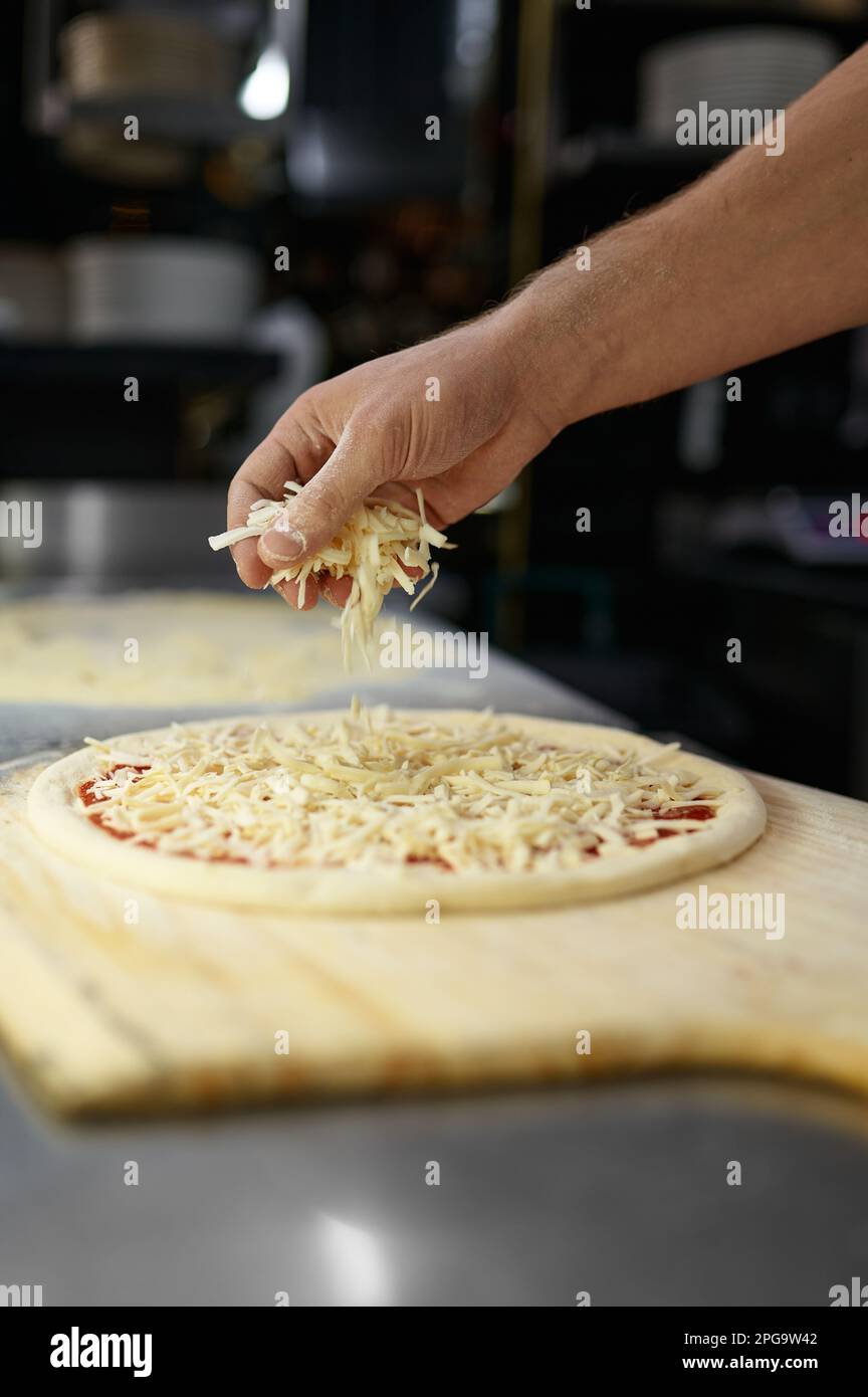 Pizza preparation process with closeup chef hands sprinkling cheese ...