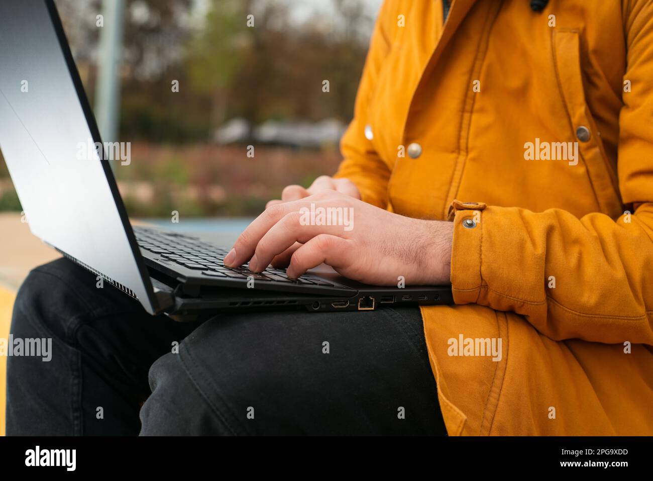 Unrecognisable businessman in orange jaket working on laptop computer ...