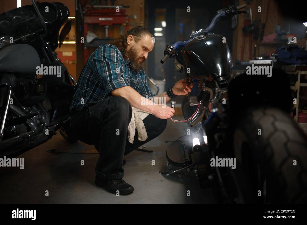 Mature man biker repairing motorcycle in garage at evening Stock Photo ...