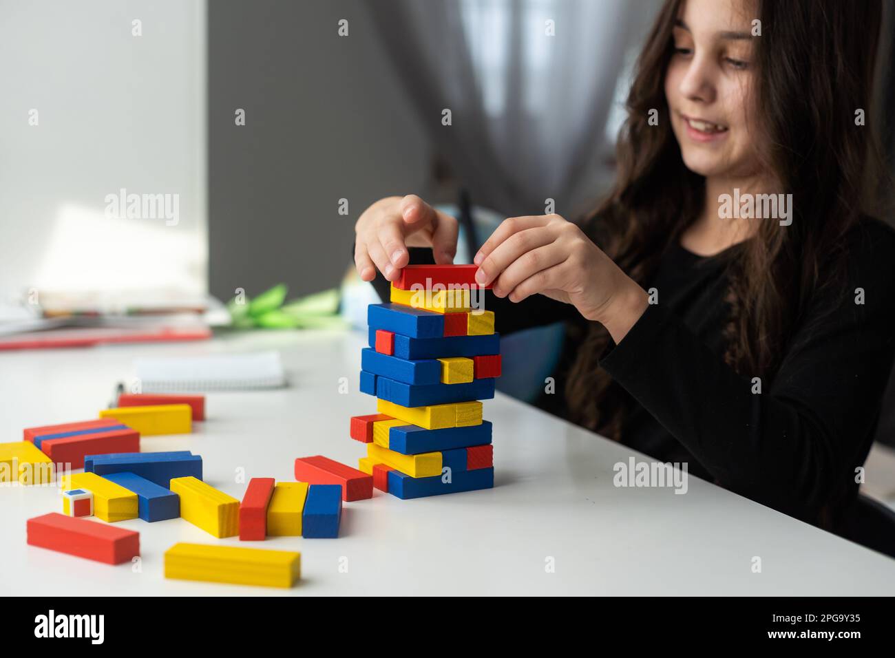 a little happy girl is playing the board game jenga at the table ...
