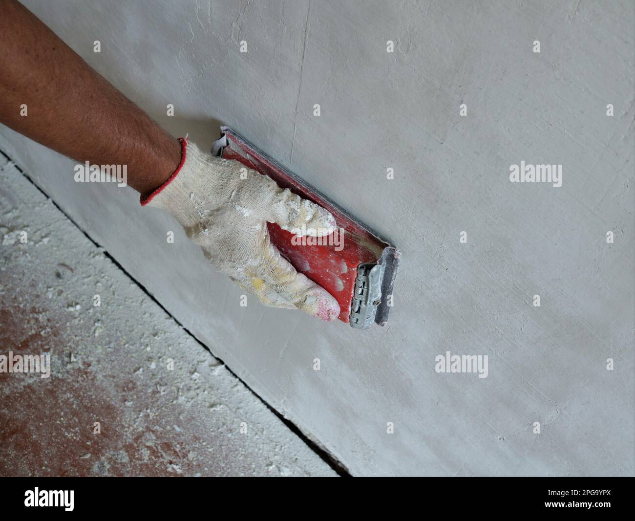 a worker's hand in a glove grinds a wall next to the floor strewn with ...