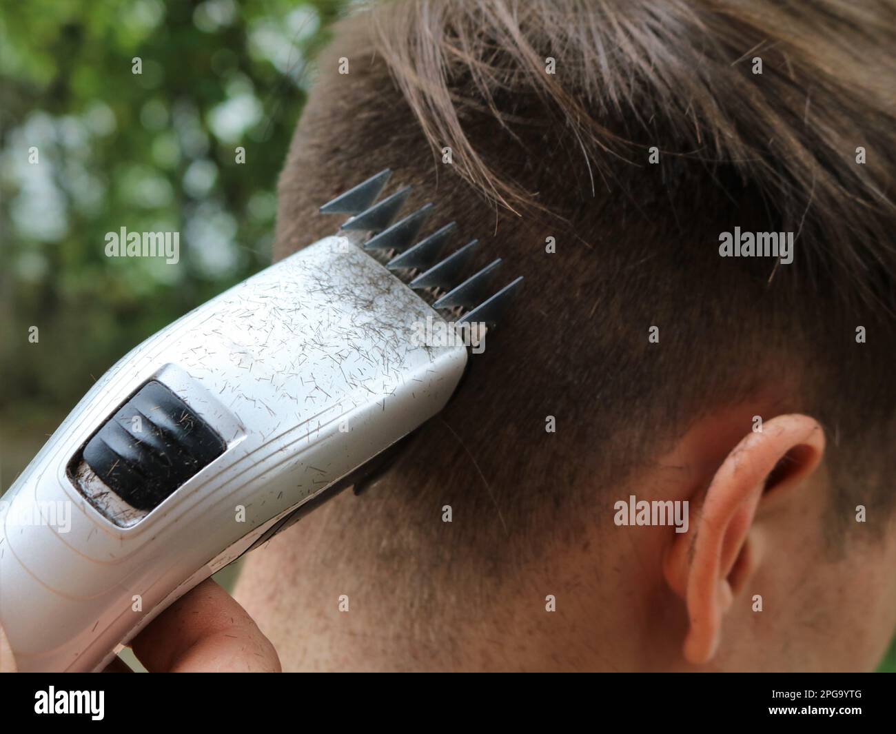 cutting the dark hair of a young man with an electric trimmer, a close ...
