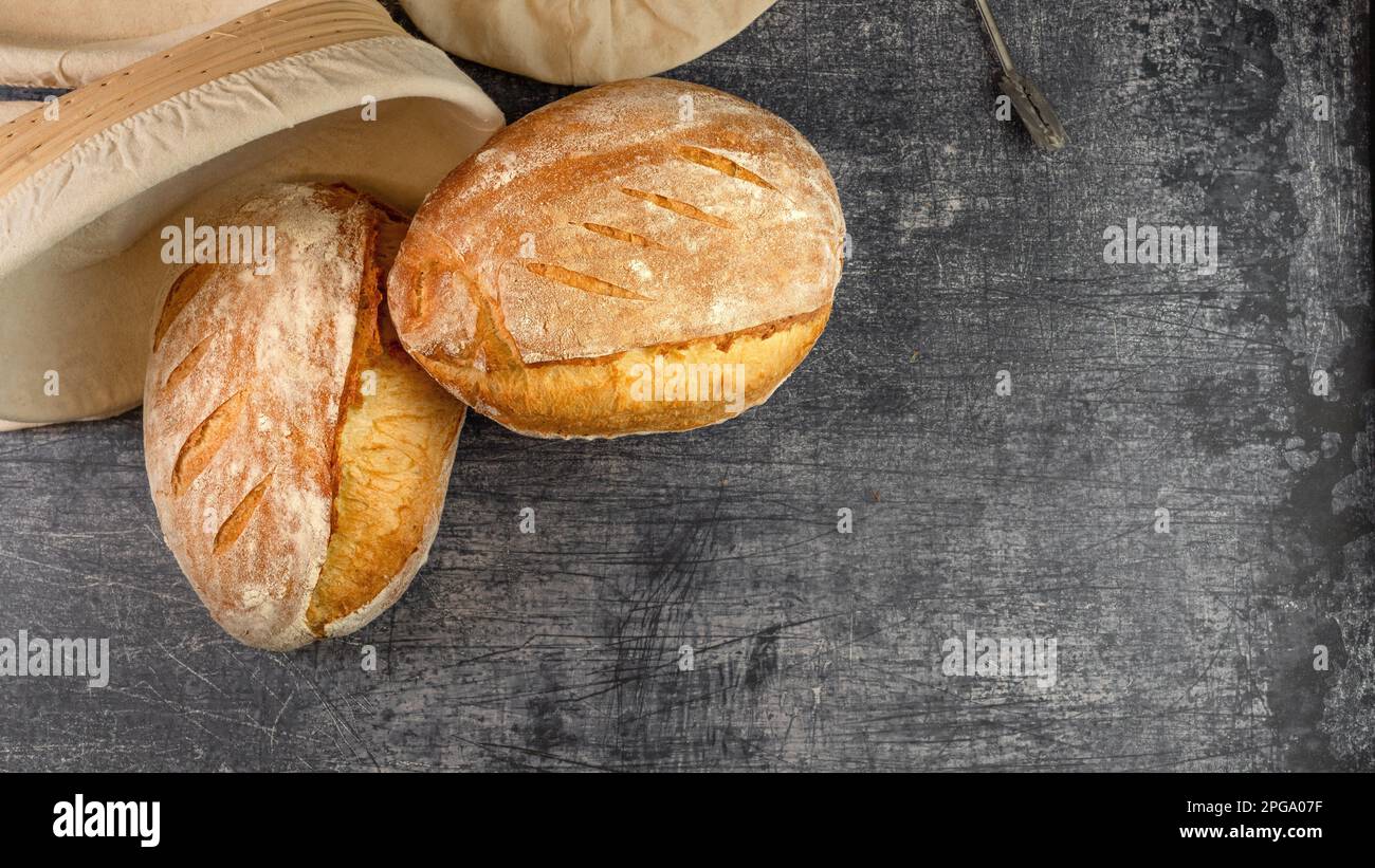 Two crusty loaves of scored bread on rustic background with a banneton ...