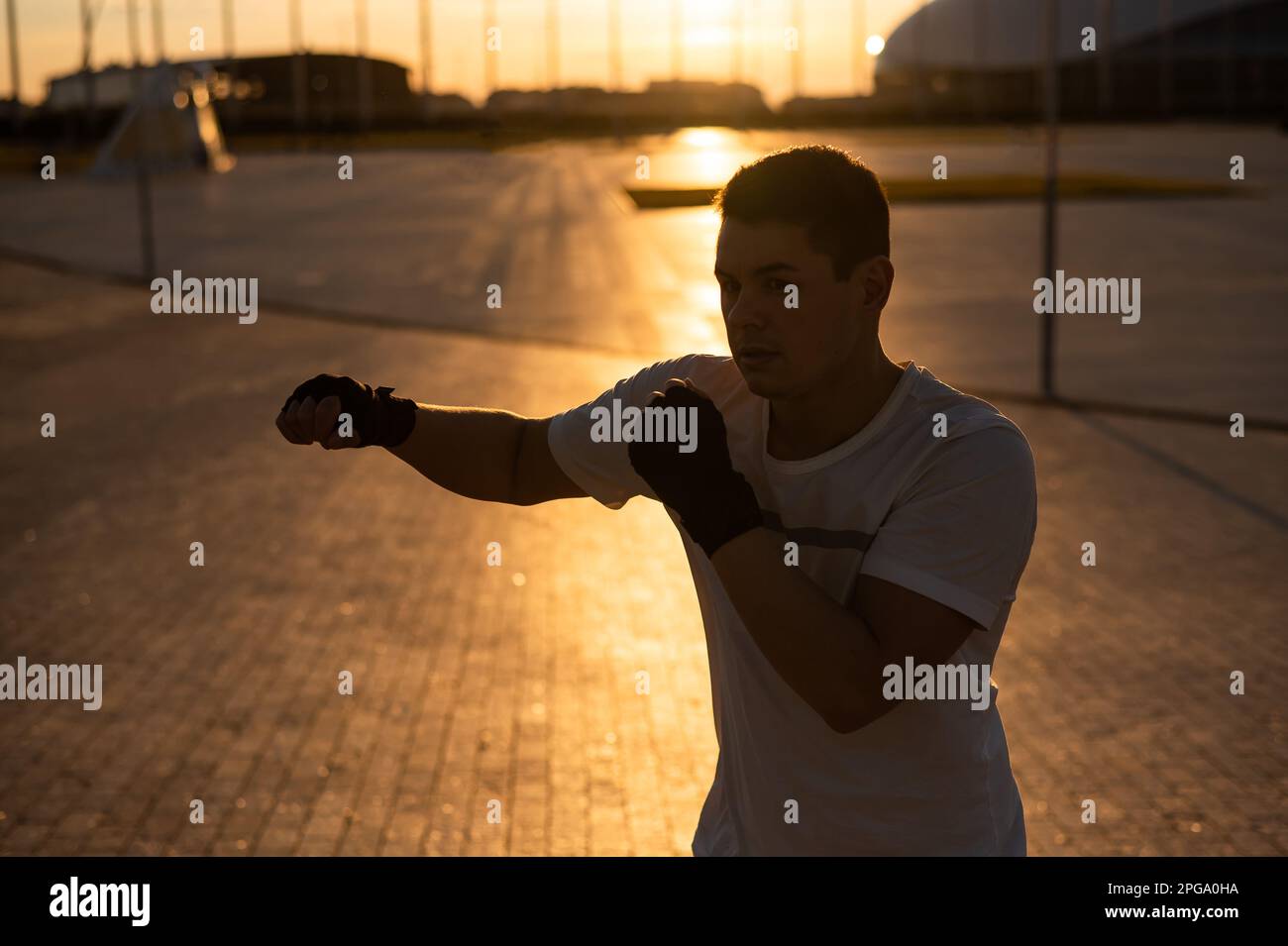 A man trains in boxing at the stadium at sunset. Athlete silhouette ...
