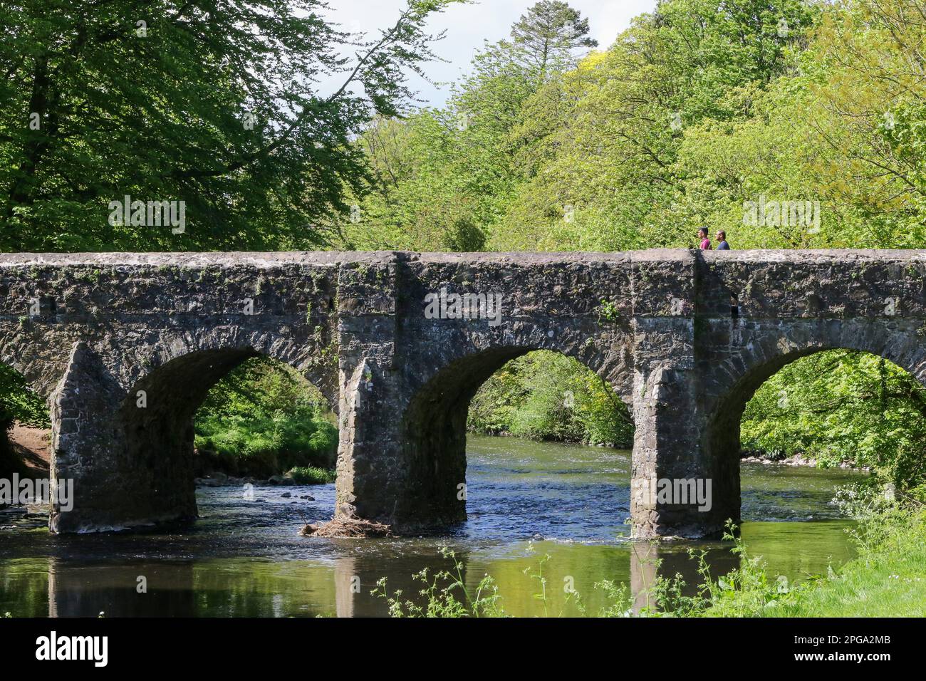 Two people standing on an arched stone bridge over Six Mile Water river ...