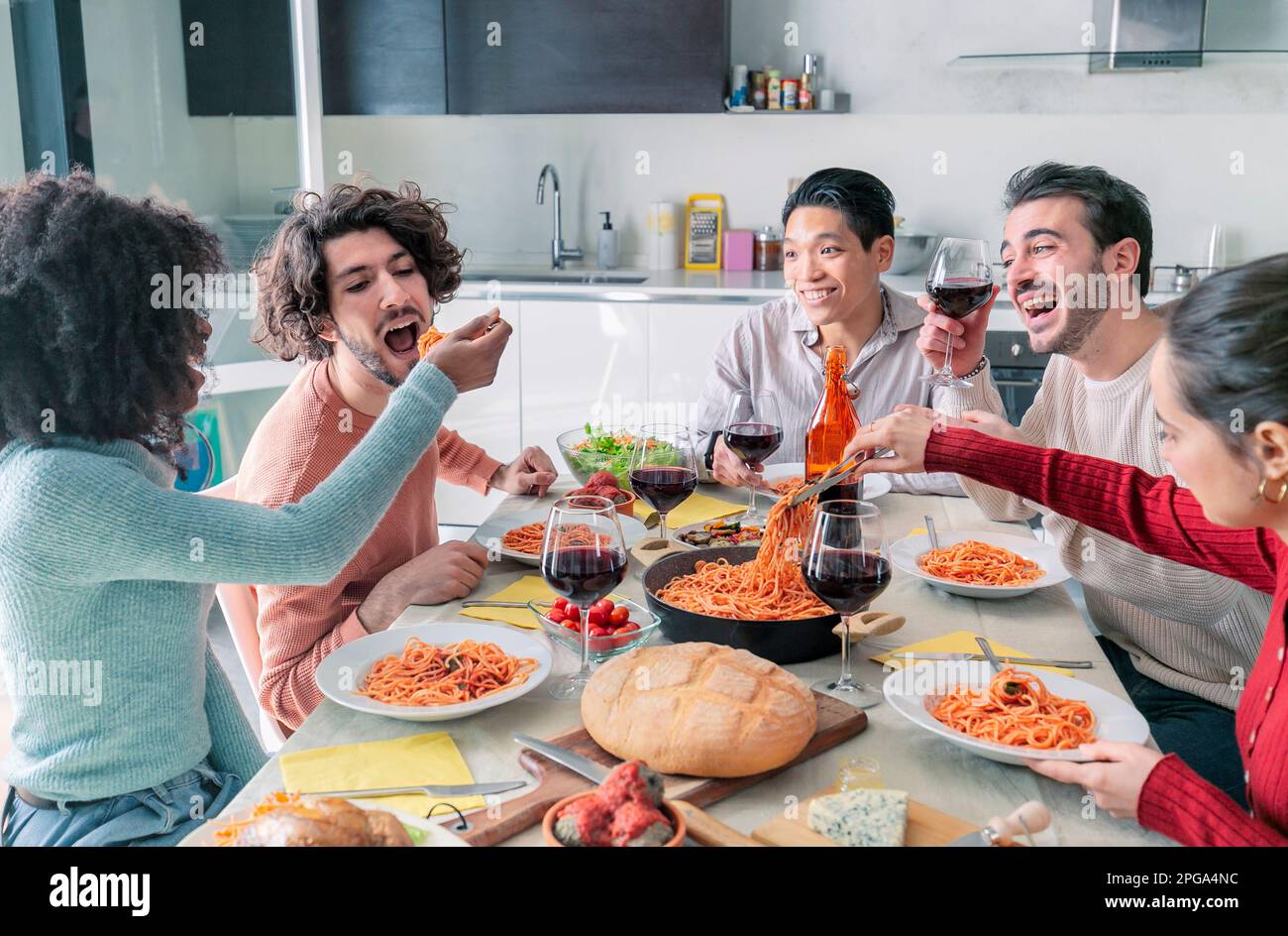 Happy young ethnic woman spoon feeding male friend with delicious pasta ...