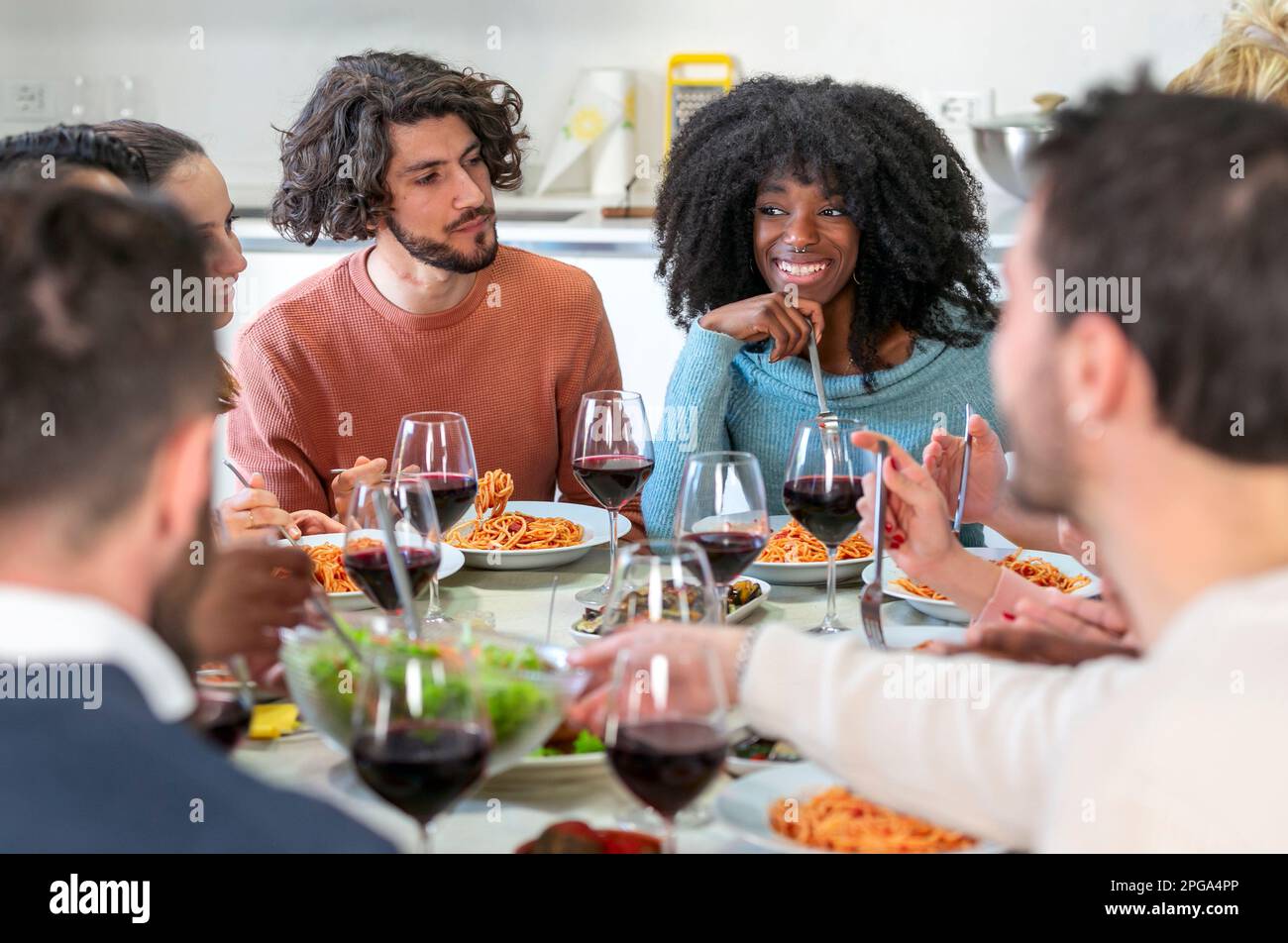 Multiethnic friends eat spaghetti with tomato sauce together in the ...
